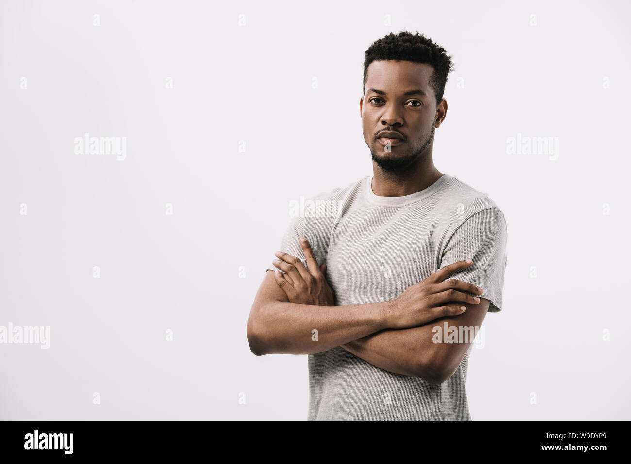 curly african american man standing with crossed arms while looking at ...