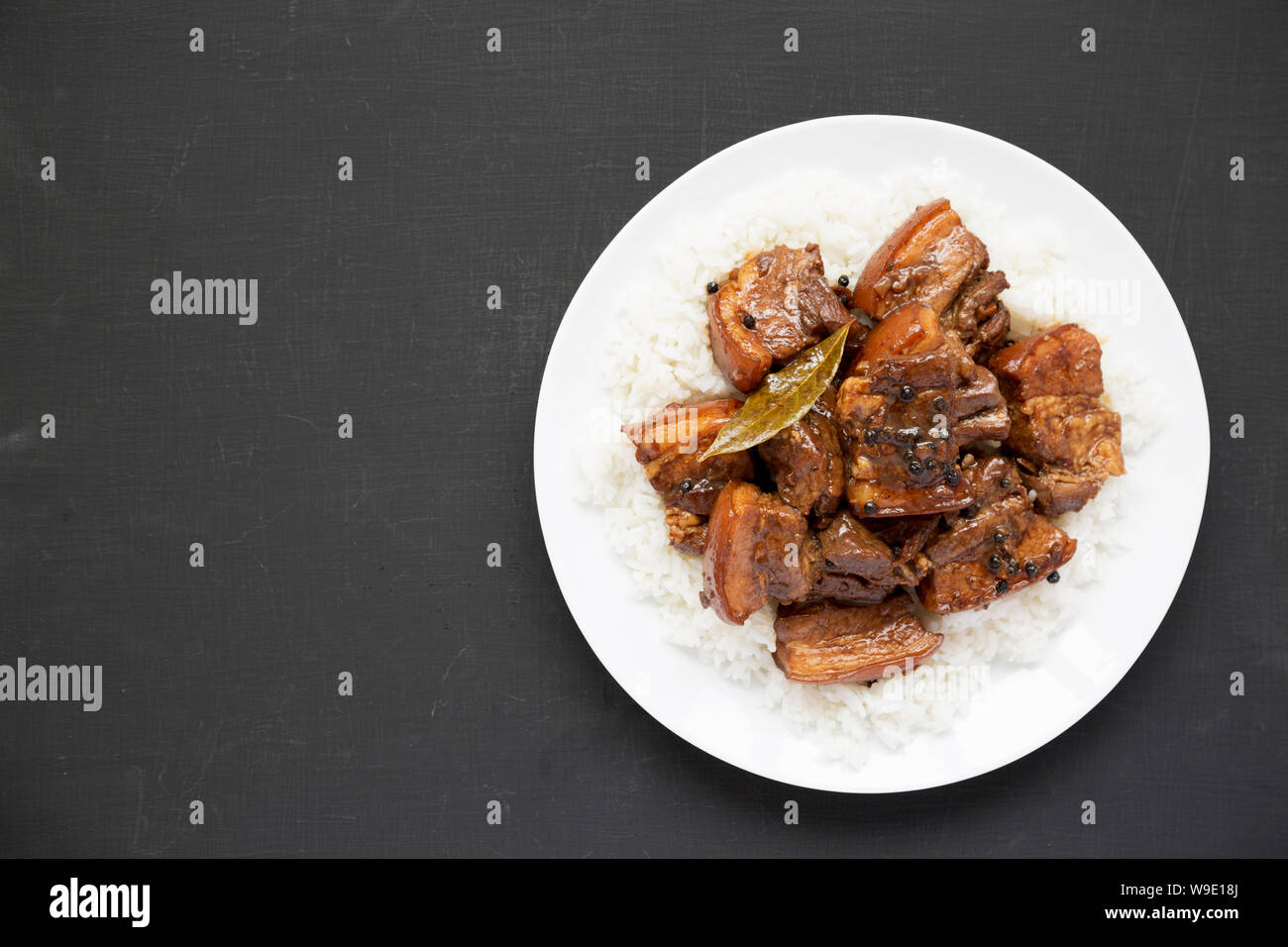 Homemade Filipino Adobo Pork with rice on a white plate over black ...