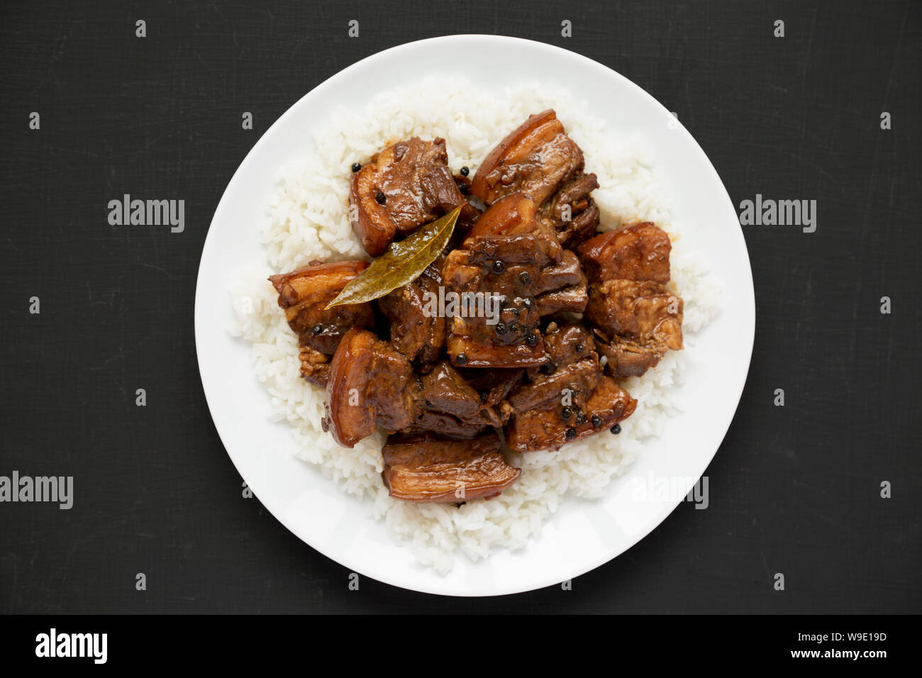 Homemade Filipino Adobo Pork with rice on a white plate over black ...