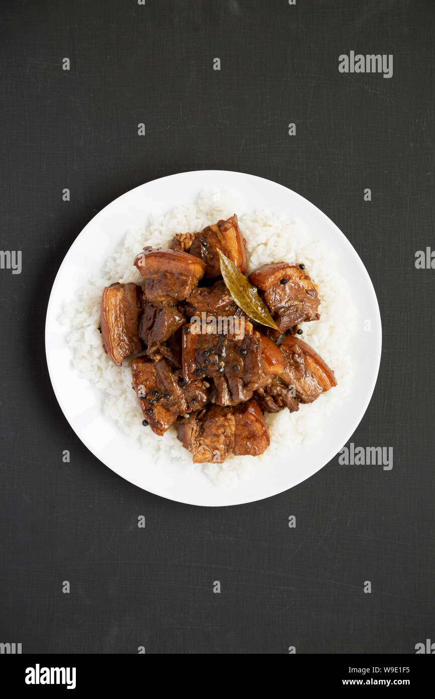 Homemade Filipino Adobo Pork with rice on a white plate over black ...