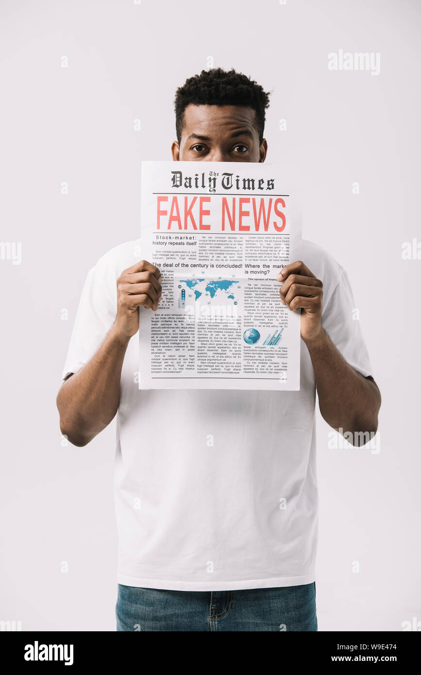 curly african american man covering face while holding newspaper with ...