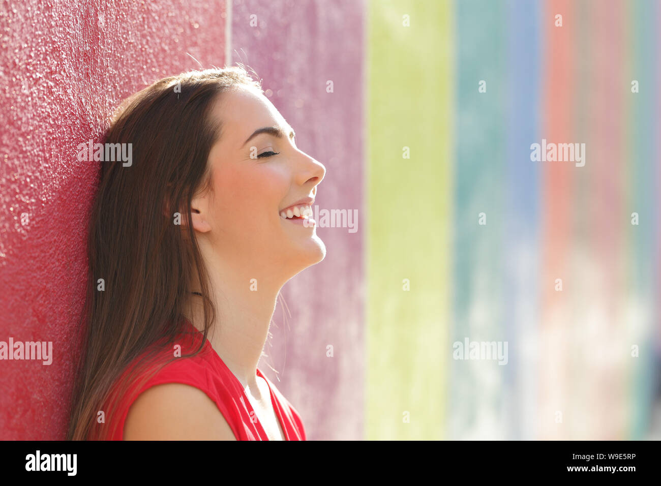 Side view portrait of a happy woman resting leaning in a colorful wall ...