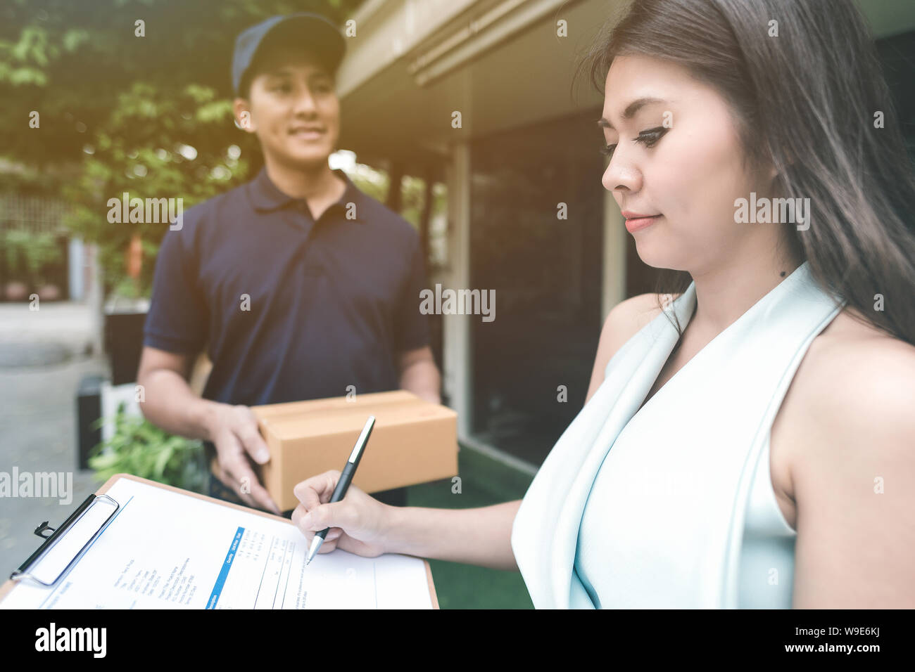 Asian delivery man smiling and giving a cardboard box to his customer ...