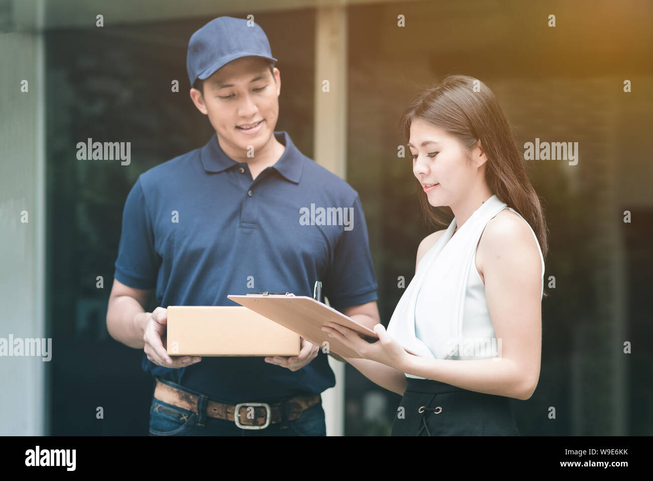 Asian delivery man smiling and giving a cardboard box to his customer ...