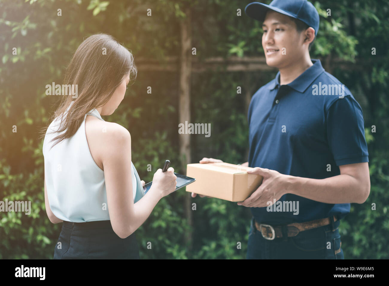 Asian delivery man smiling and giving a cardboard box to his customer ...