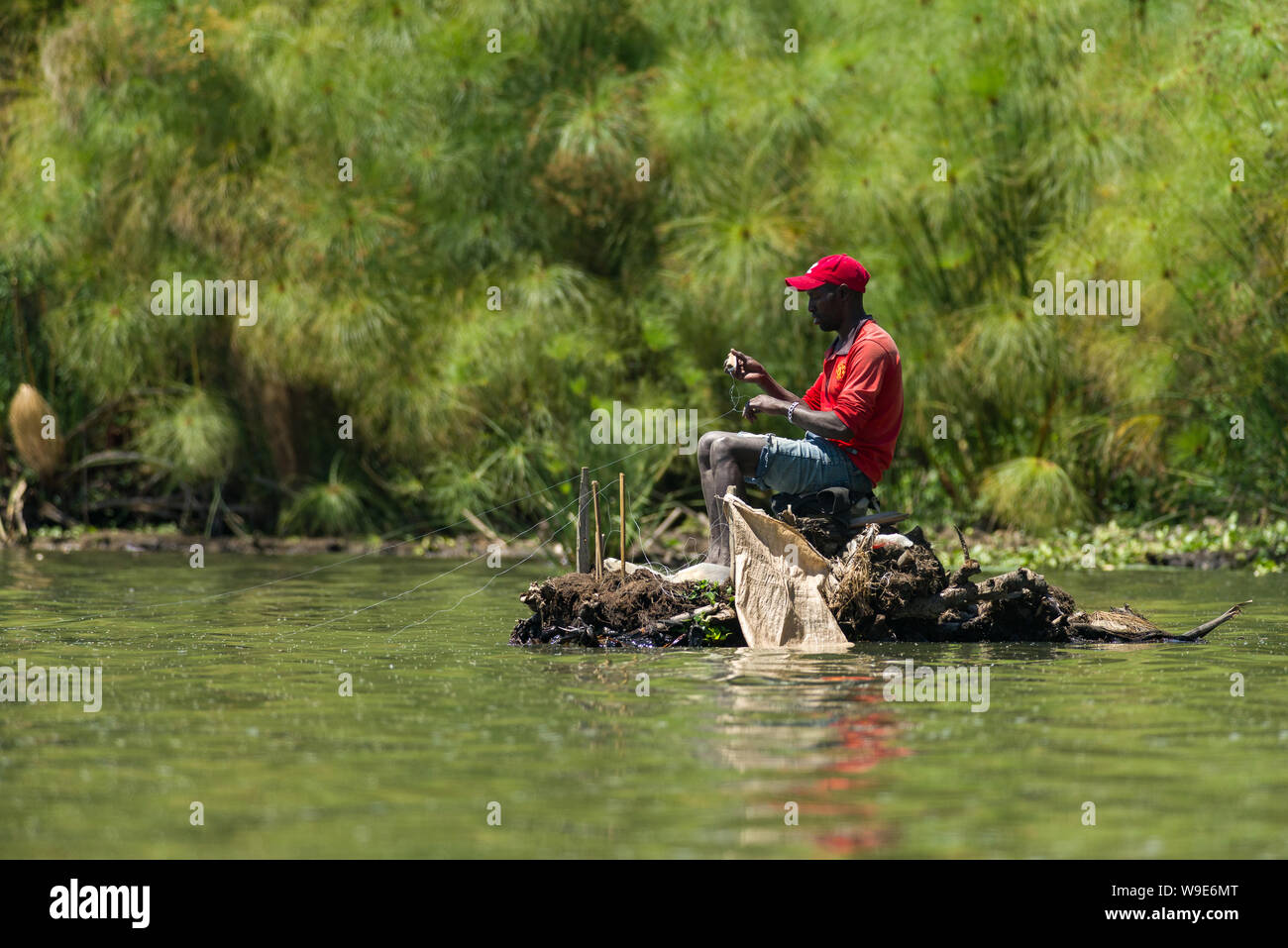 A lone Kenyan fisherman sits on a mound of earth fishing in lake ...