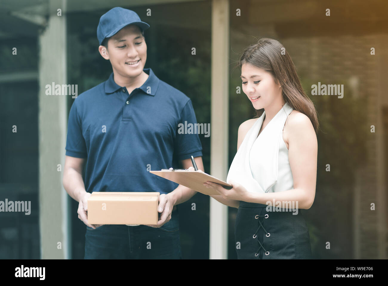 Asian delivery man smiling and giving a cardboard box to his customer ...