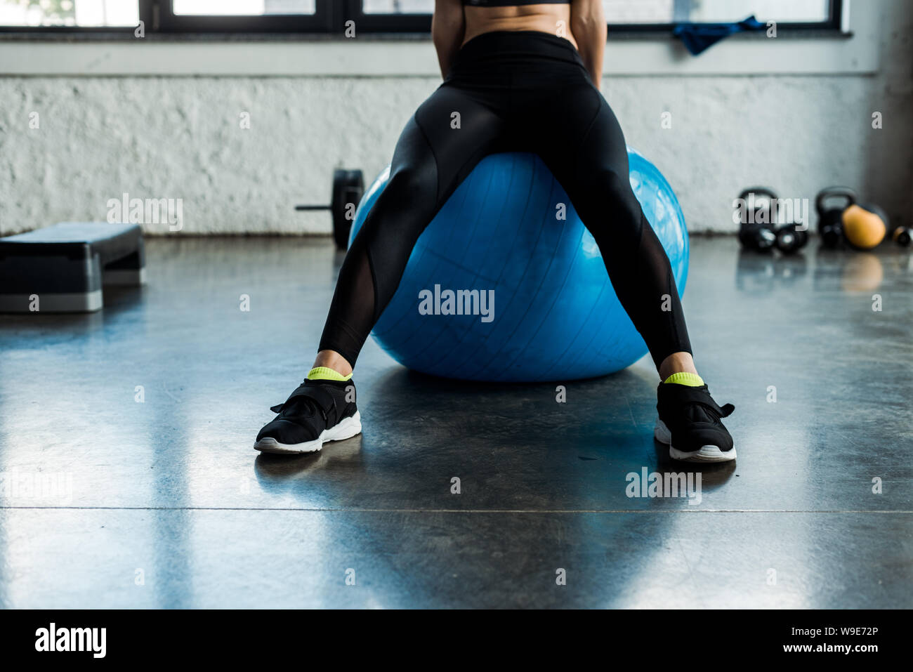 cropped view of girl sitting on blue fitness ball in sports center ...