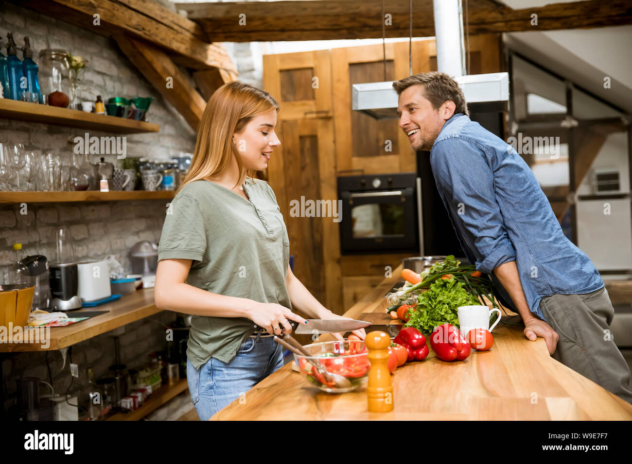 Beautiful young couple smiling while cooking in kitchen at loft ...