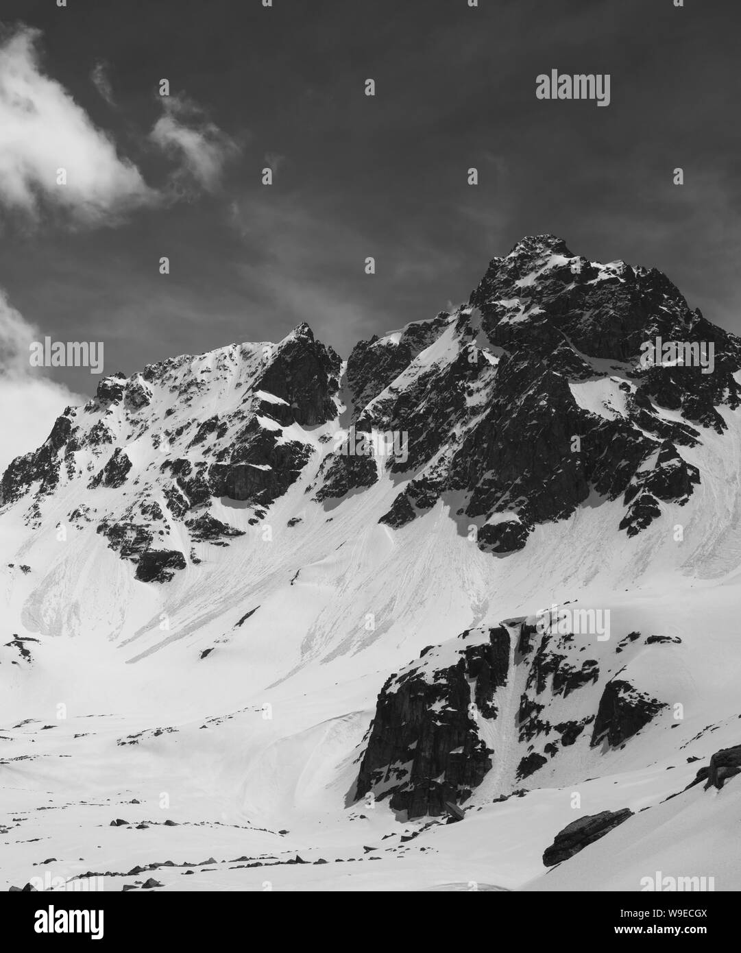 Snowy sunlit mountains with traces from avalanche and cloudy sky in ...