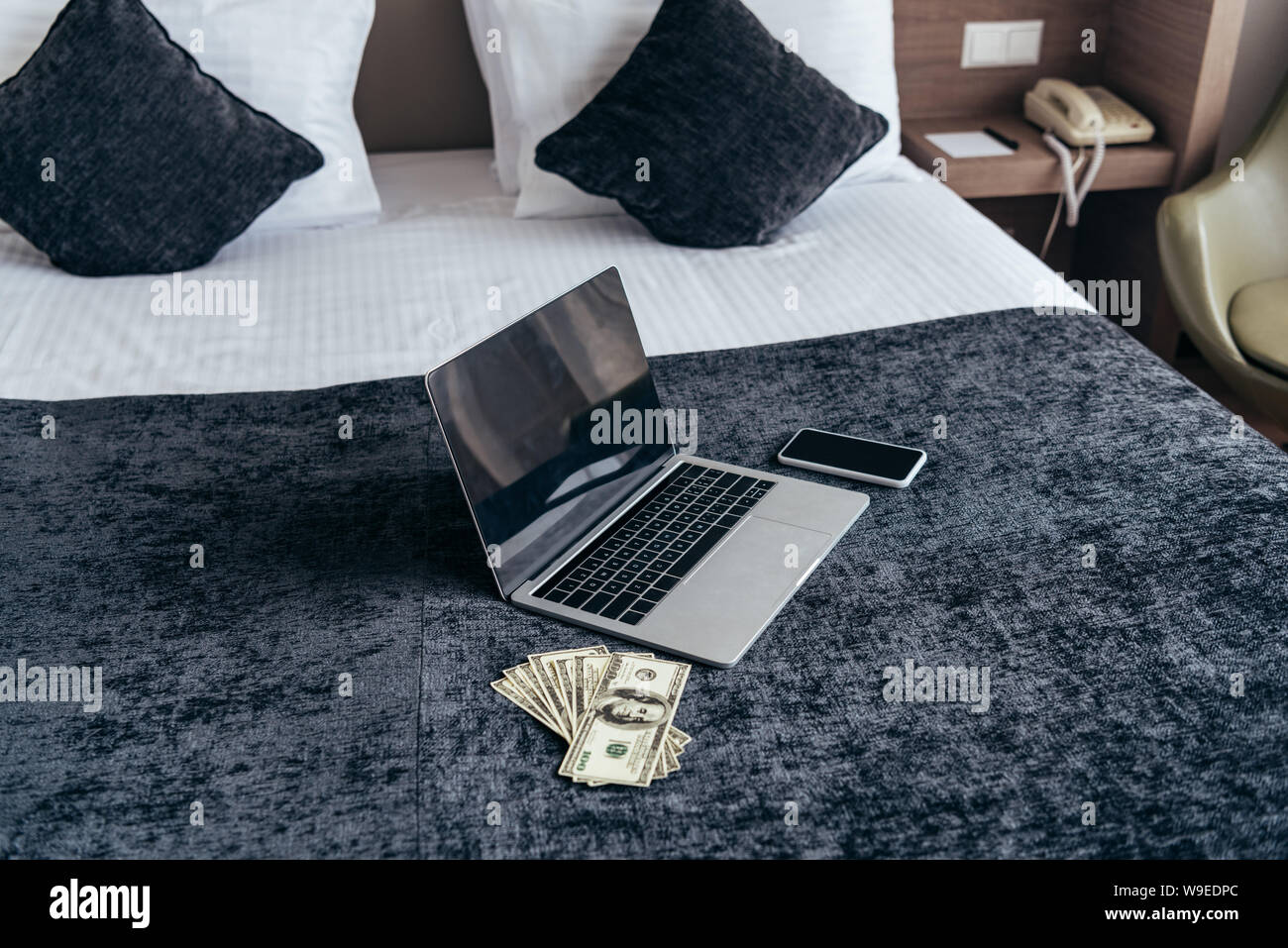 laptop with blank screen, smartphone and dollar banknotes on bed in ...
