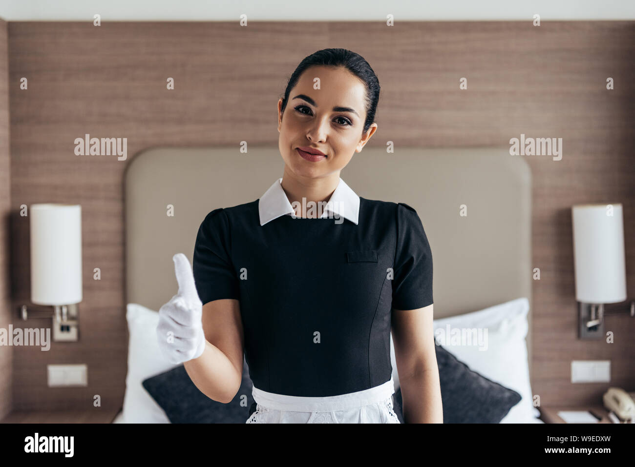 front view of pretty smiling maid in white glove and apron looking at ...