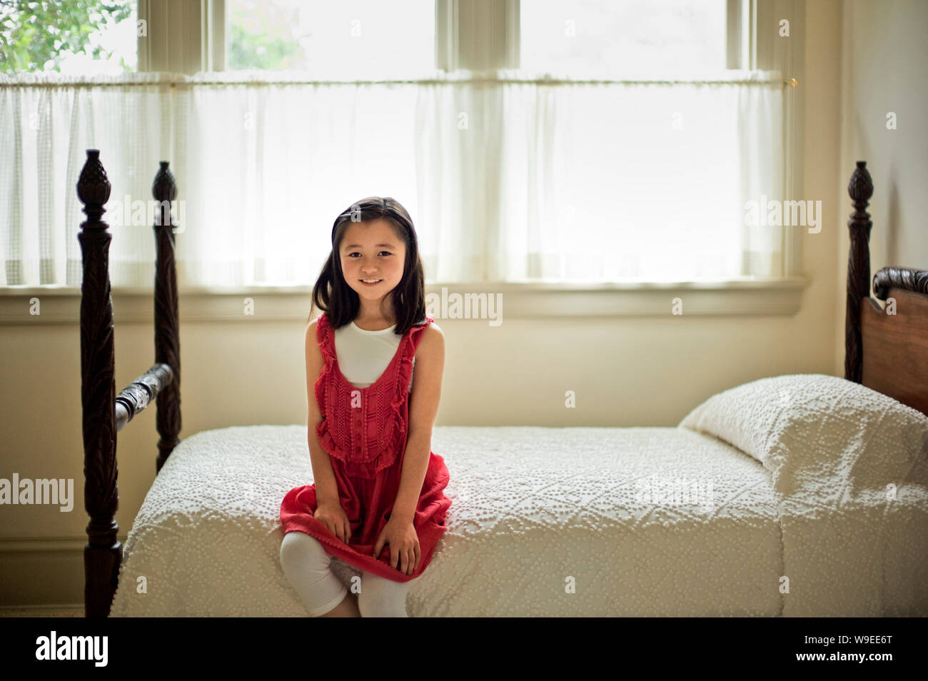 Young girl sits on the edge of a bed and smiles as she poses for a ...