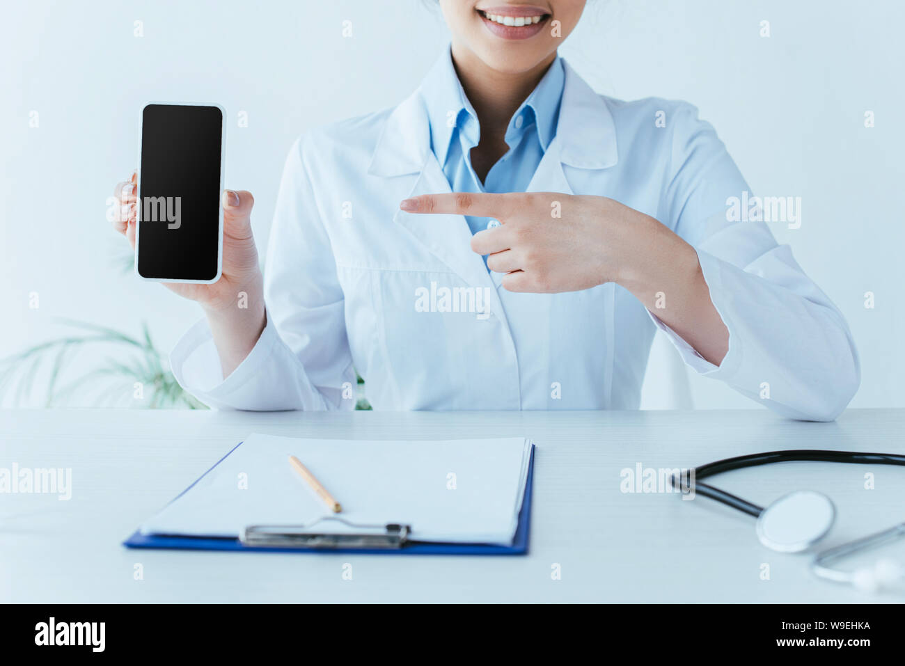 partial view of smiling latin doctor pointing with finger at smartphone ...