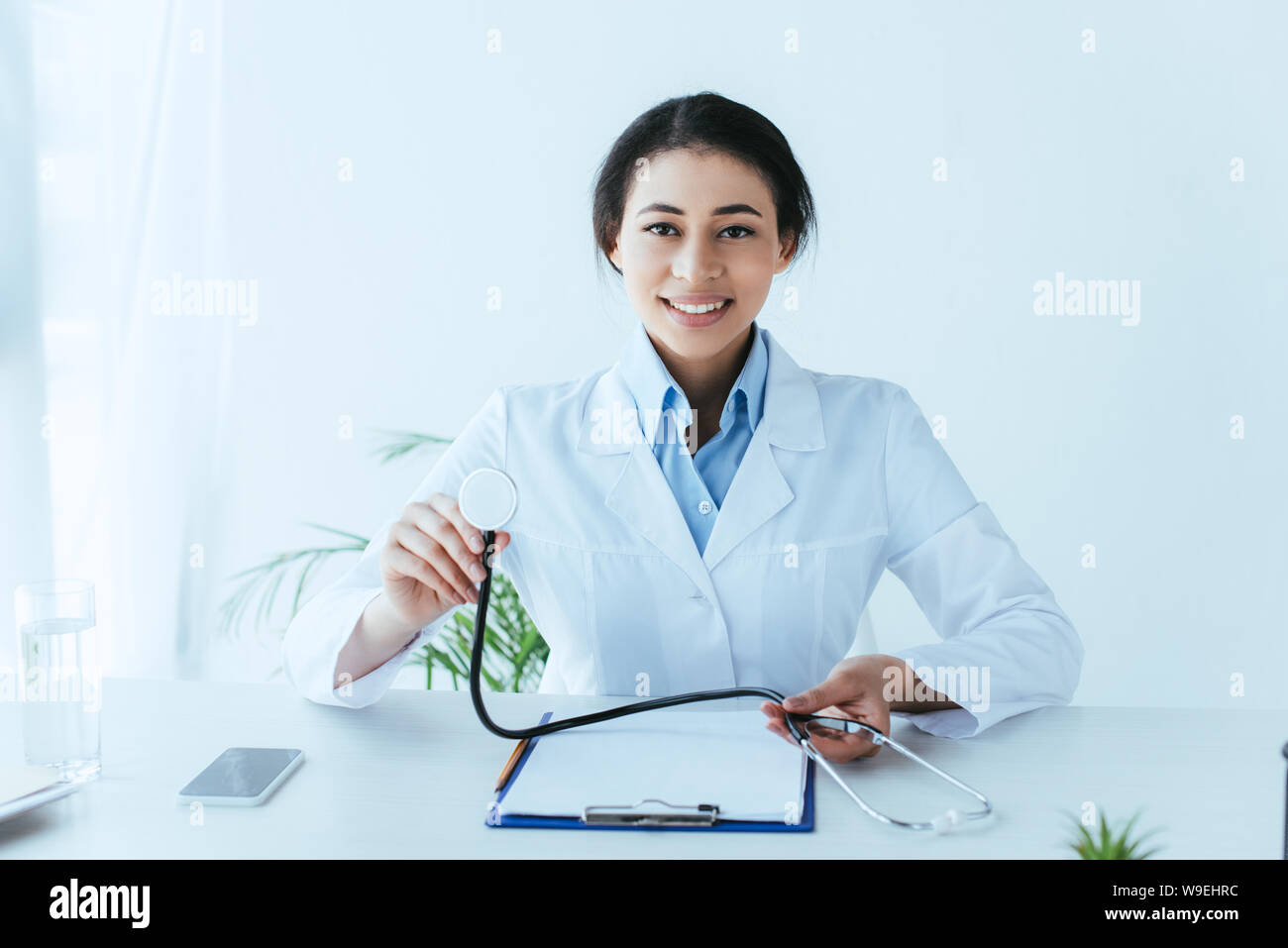 smiling latin doctor holding stethoscope and smiling at camera while ...