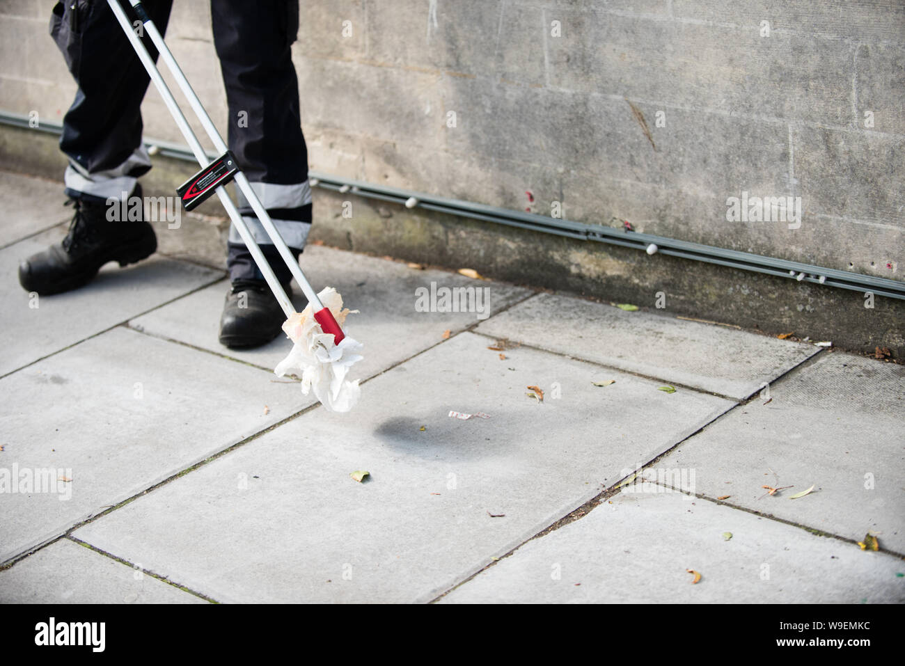 Street cleansing worker sweeps up fallen leaves on a pavement keeping ...