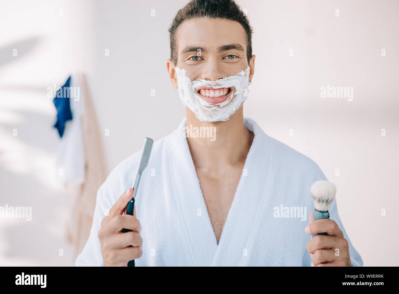 handsome young man with shaving cream on face holding razor blade and ...