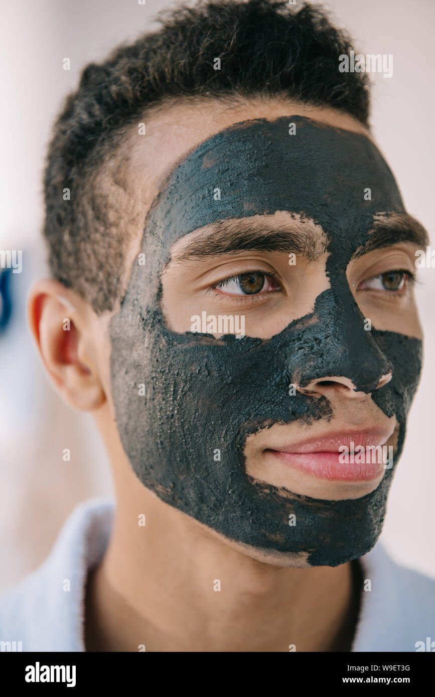 portrait shot of handsome man with grey clay mask on face looking away ...