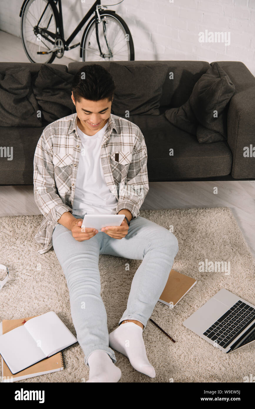 overhead view of smiling asian man sitting on floor near couch and ...