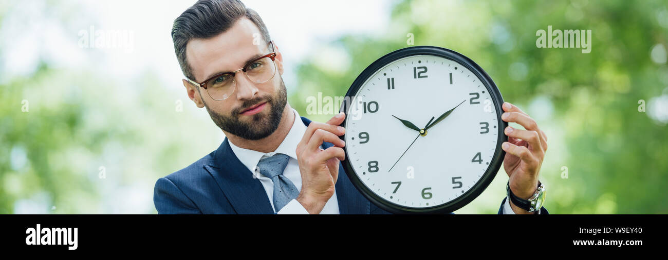 panoramic shot of young man holding clock and looking at camera Stock ...
