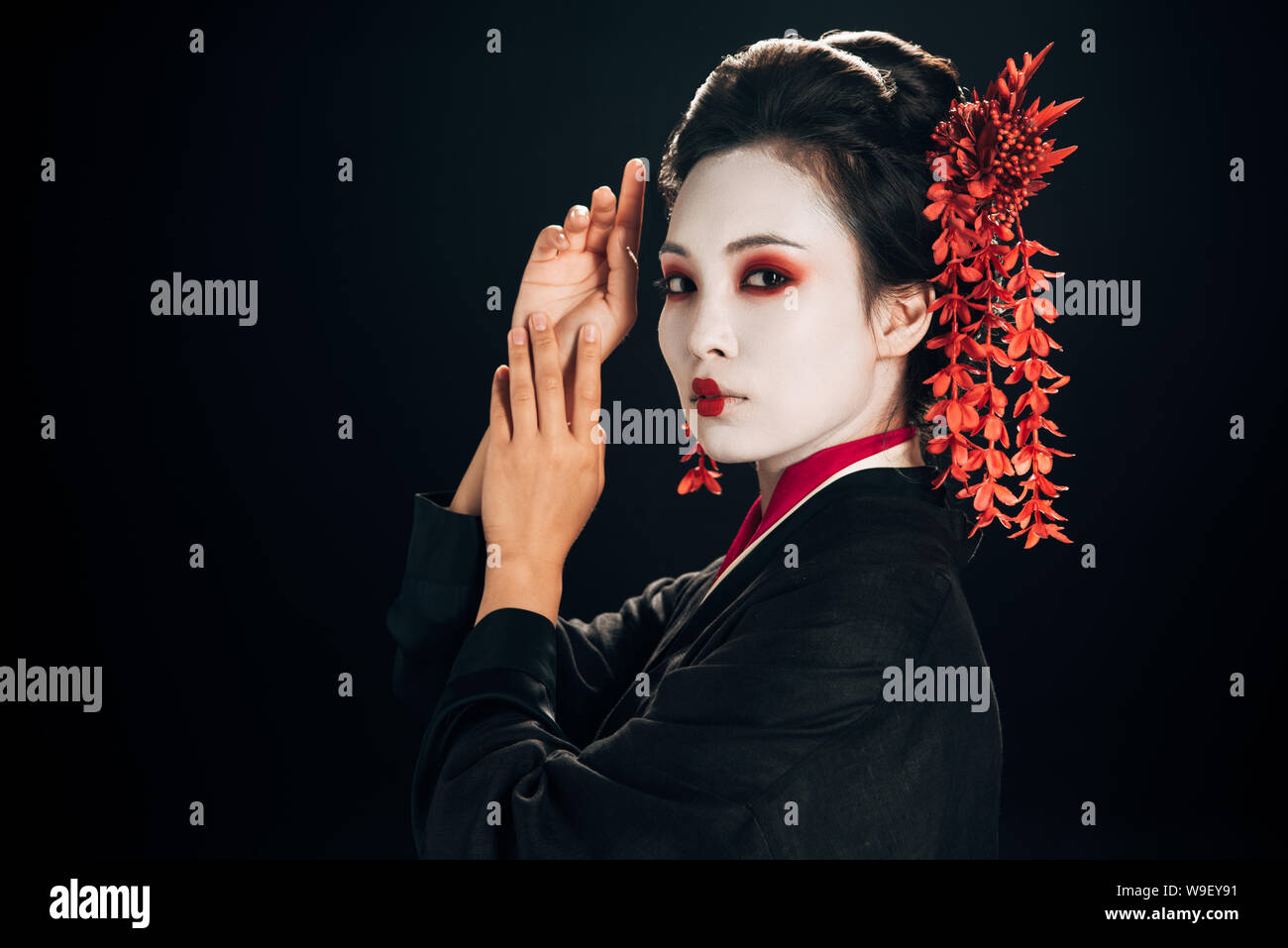 side view of beautiful geisha in black and red kimono and flowers in ...