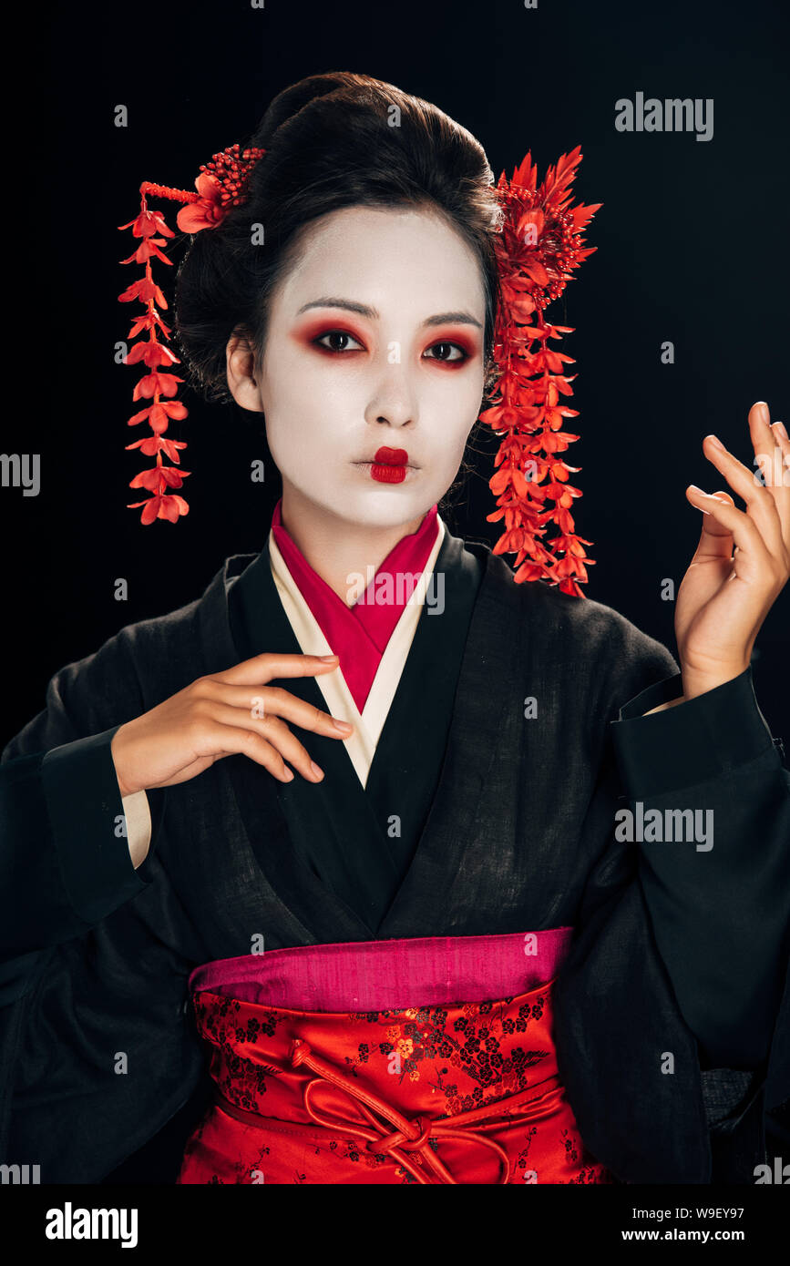 geisha in black and red kimono and flowers in hair gesturing isolated ...