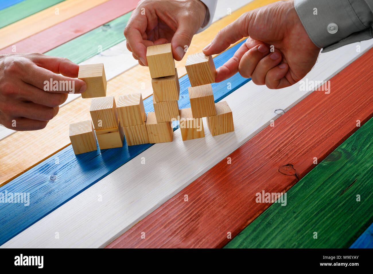 Three hands of businessmen stacking cubes to form a structure in a ...