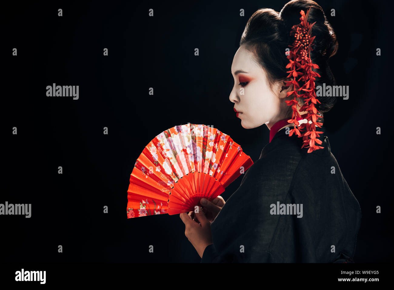 side view of beautiful geisha in black kimono with red flowers in hair ...
