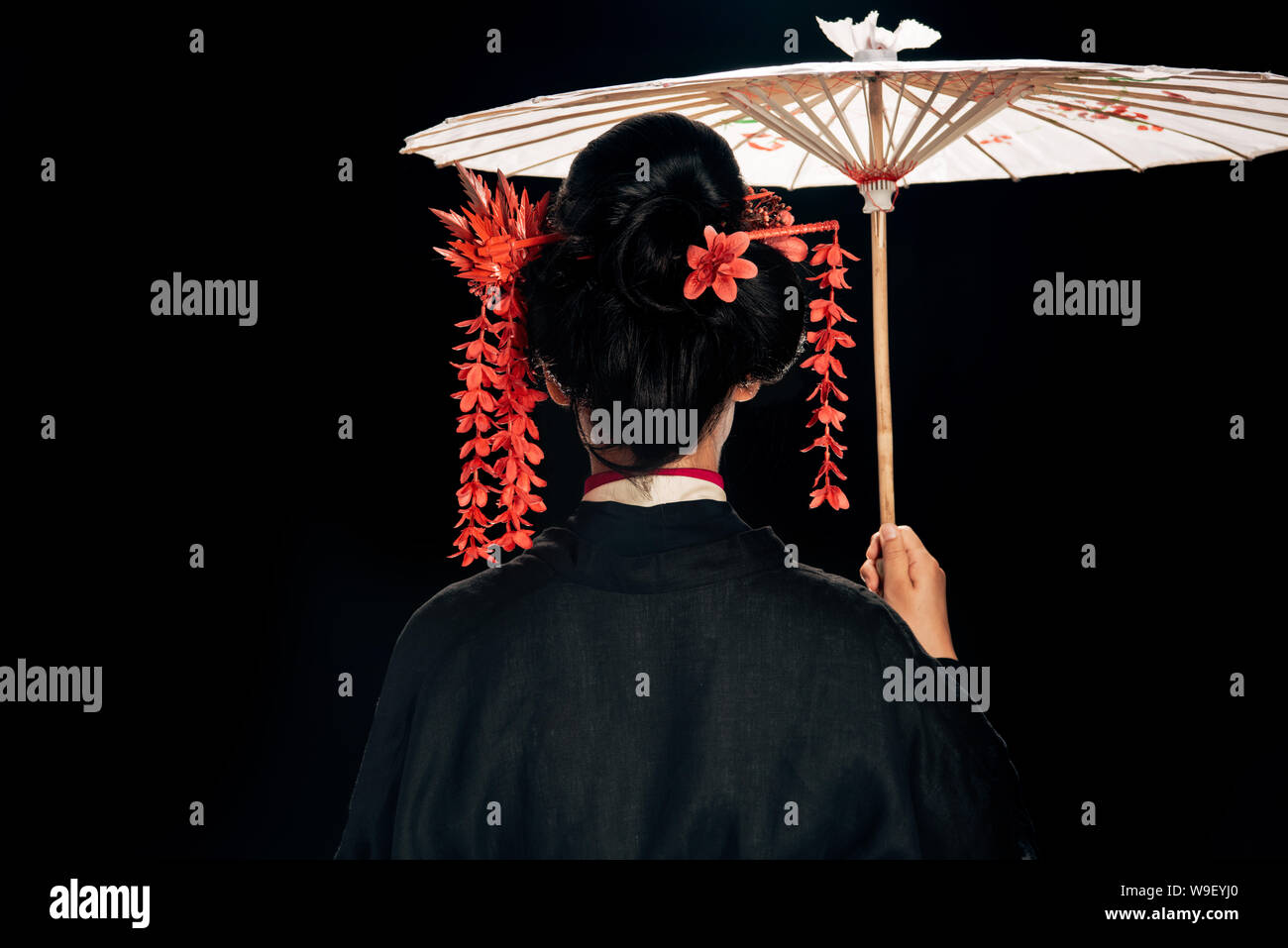 back view of beautiful geisha in black kimono with red flowers in hair ...