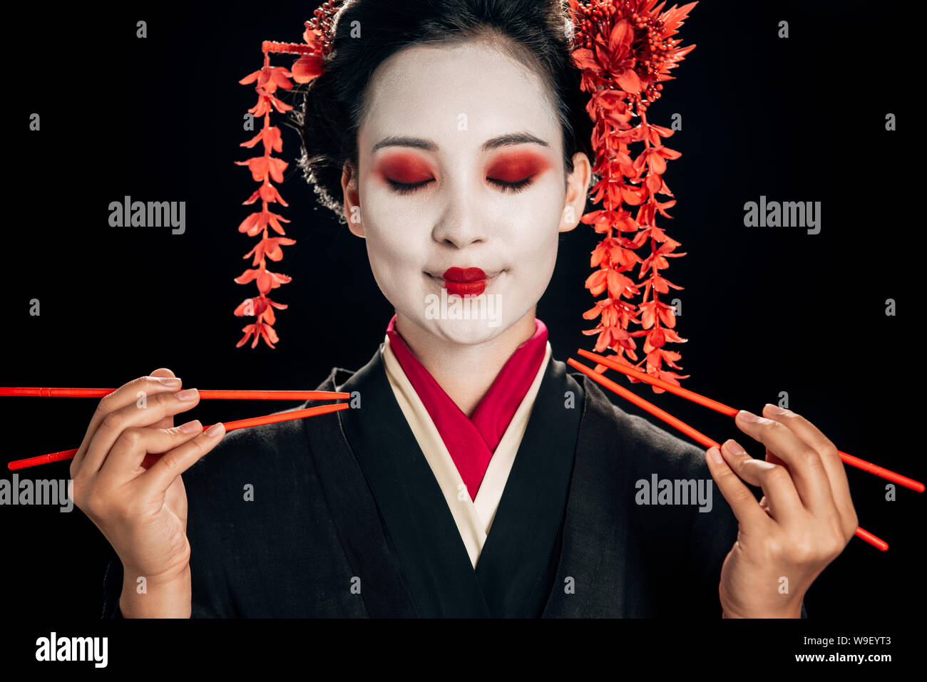 smiling beautiful geisha in black kimono with red flowers in hair and ...