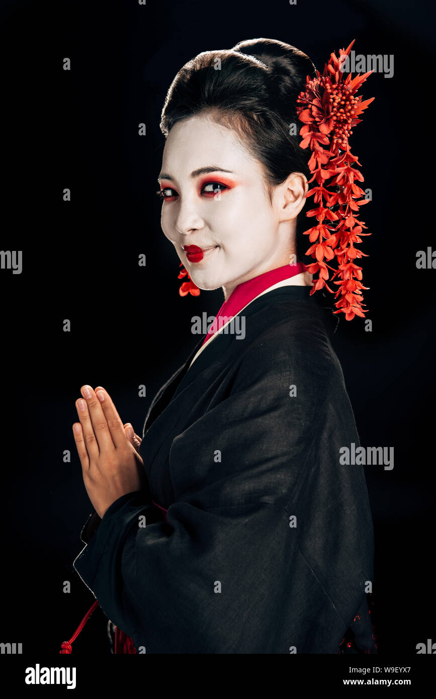 side view of happy beautiful geisha in black and red kimono and flowers ...