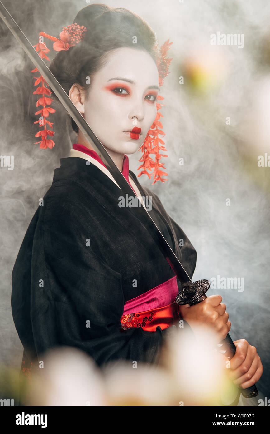 selective focus of serious geisha in black kimono holding katana in ...