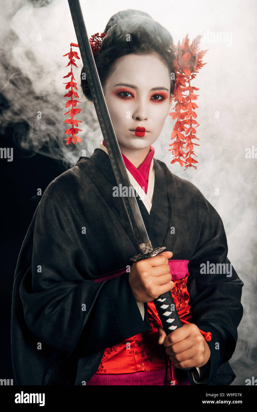 confident beautiful geisha in black kimono holding katana in smoke ...