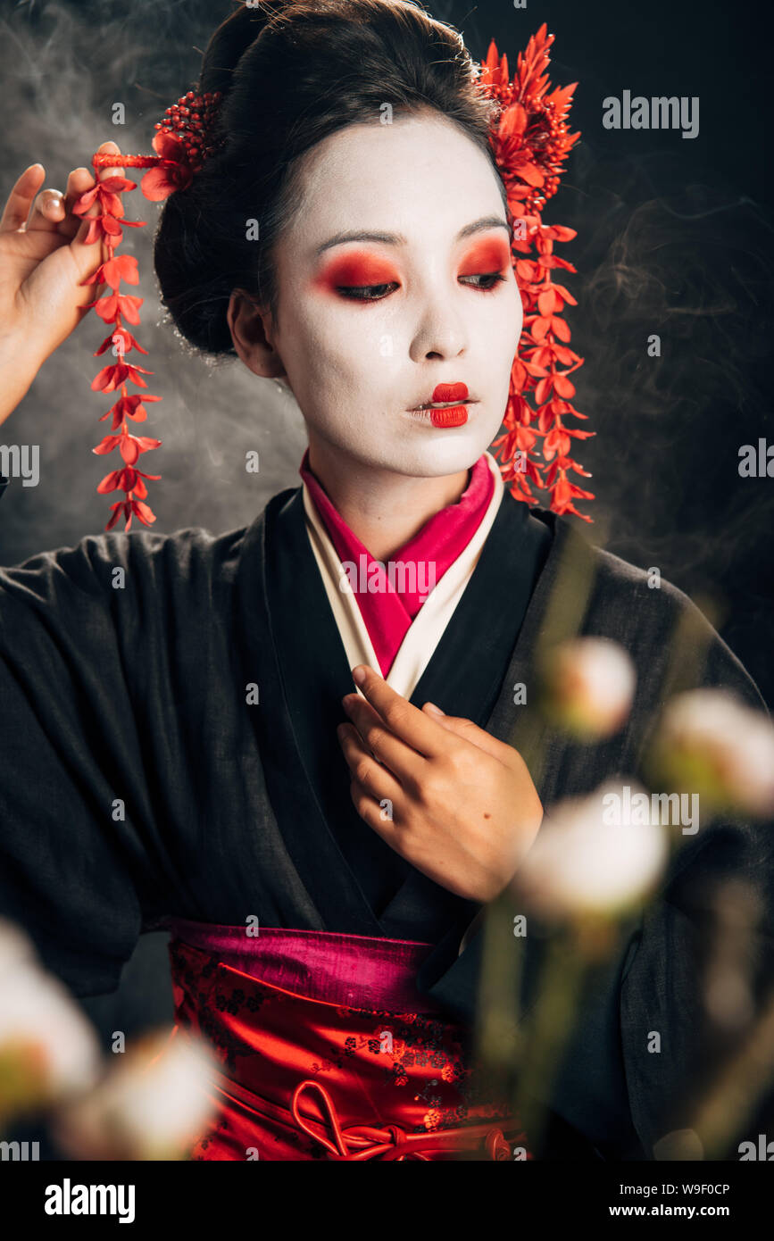 selective focus of geisha in black kimono with red flowers in hair and ...