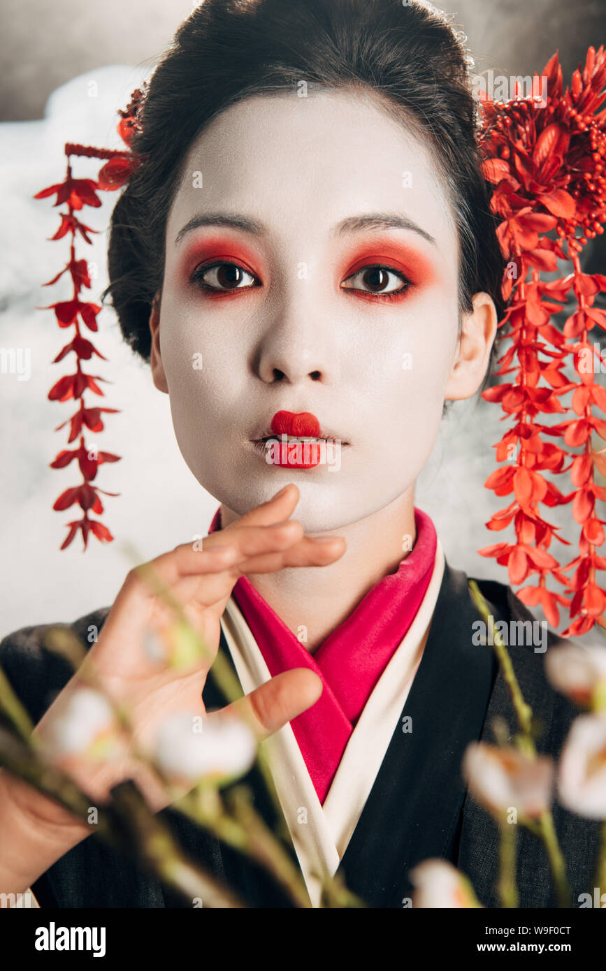 portrait of beautiful geisha in black kimono with red flowers in hair ...