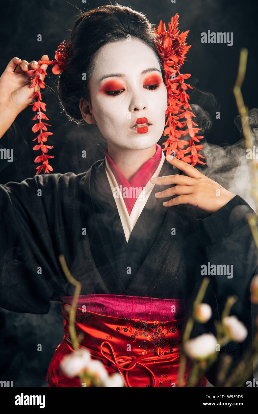 selective focus of beautiful geisha in black kimono with red flowers in ...