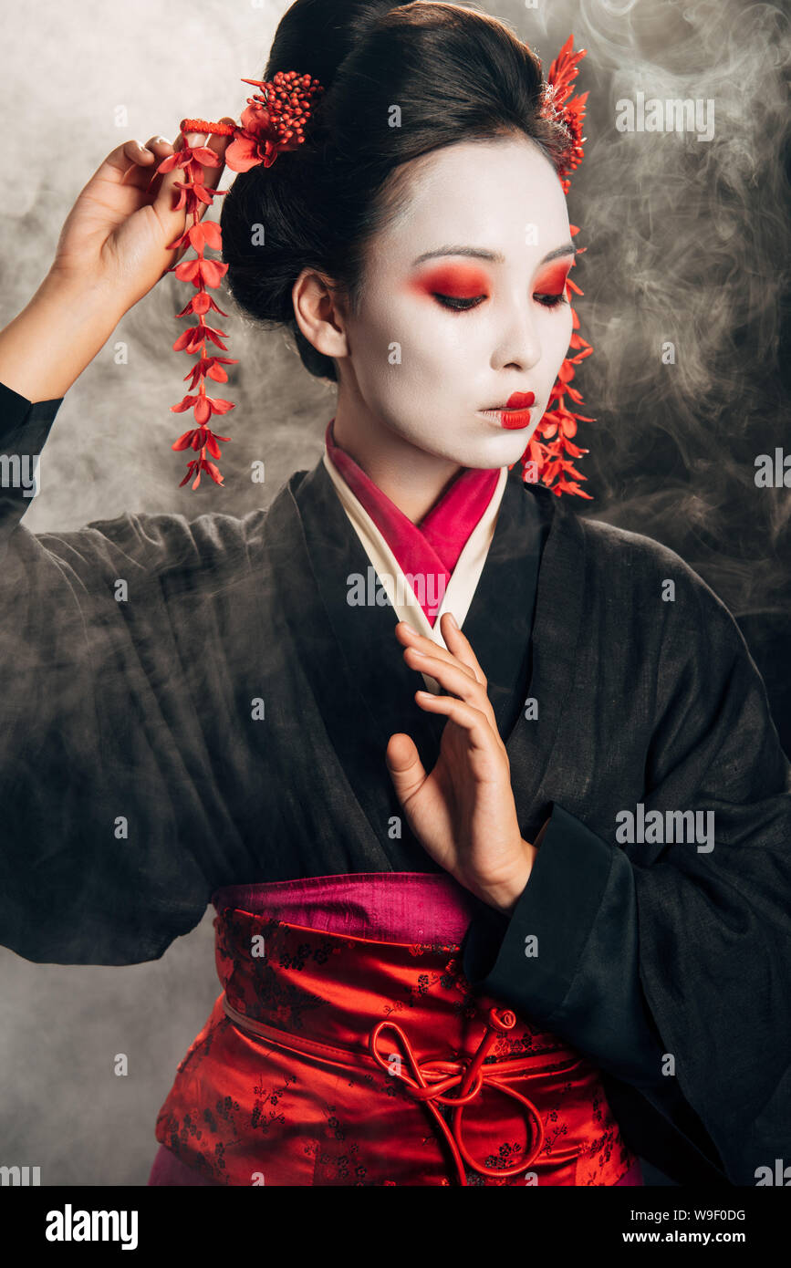 geisha in black kimono with red flowers in hair gesturing on black ...