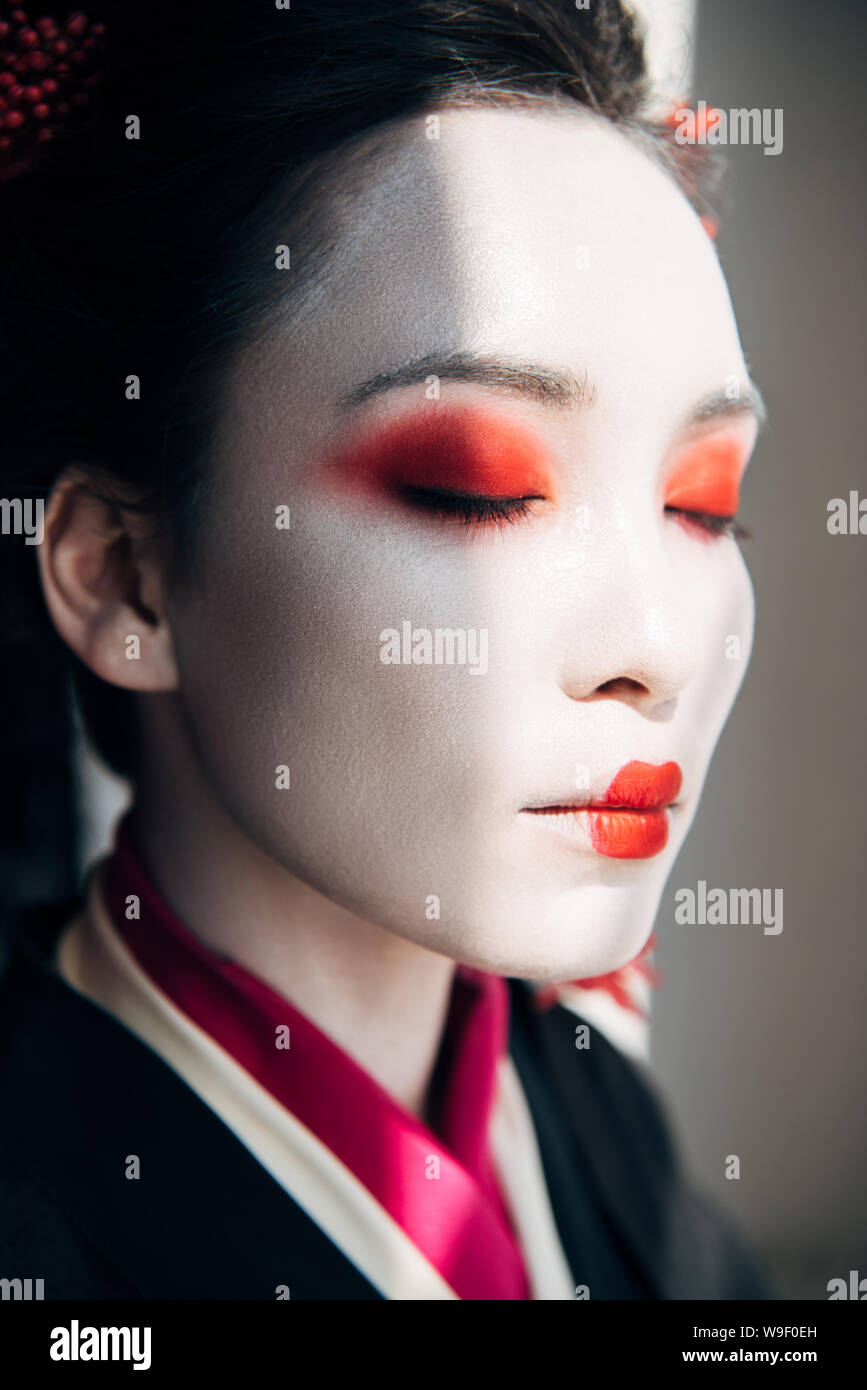 portrait of beautiful geisha with red and white makeup with closed eyes ...