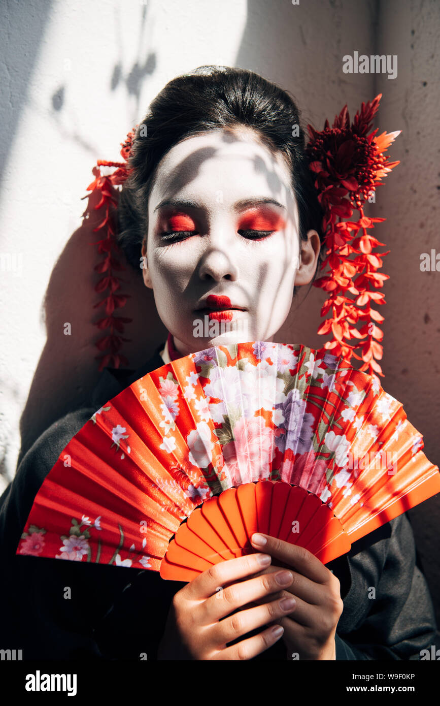 portrait of beautiful geisha with red and white makeup holding hand fan ...