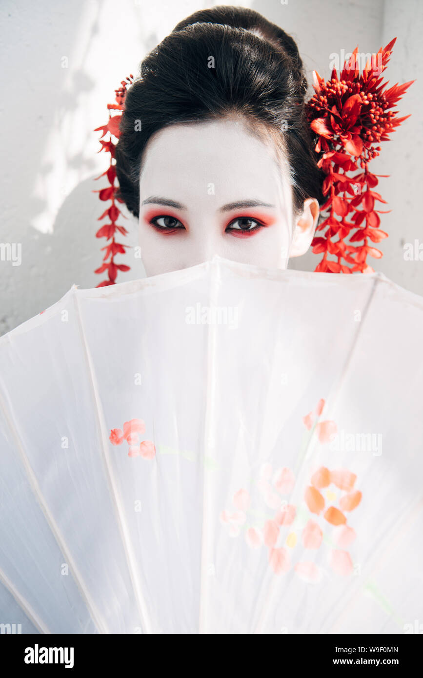 beautiful geisha with red and white makeup holding umbrella in sunlight ...