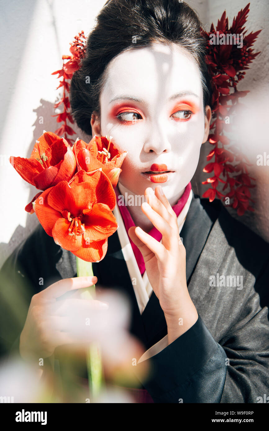 selective focus of sakura branches and beautiful geisha holding red ...