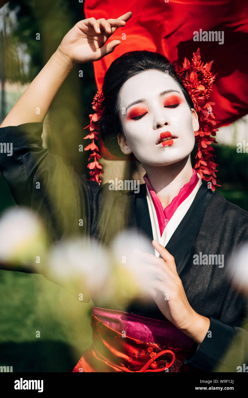 selective focus of tree branches and beautiful gesturing geisha with ...