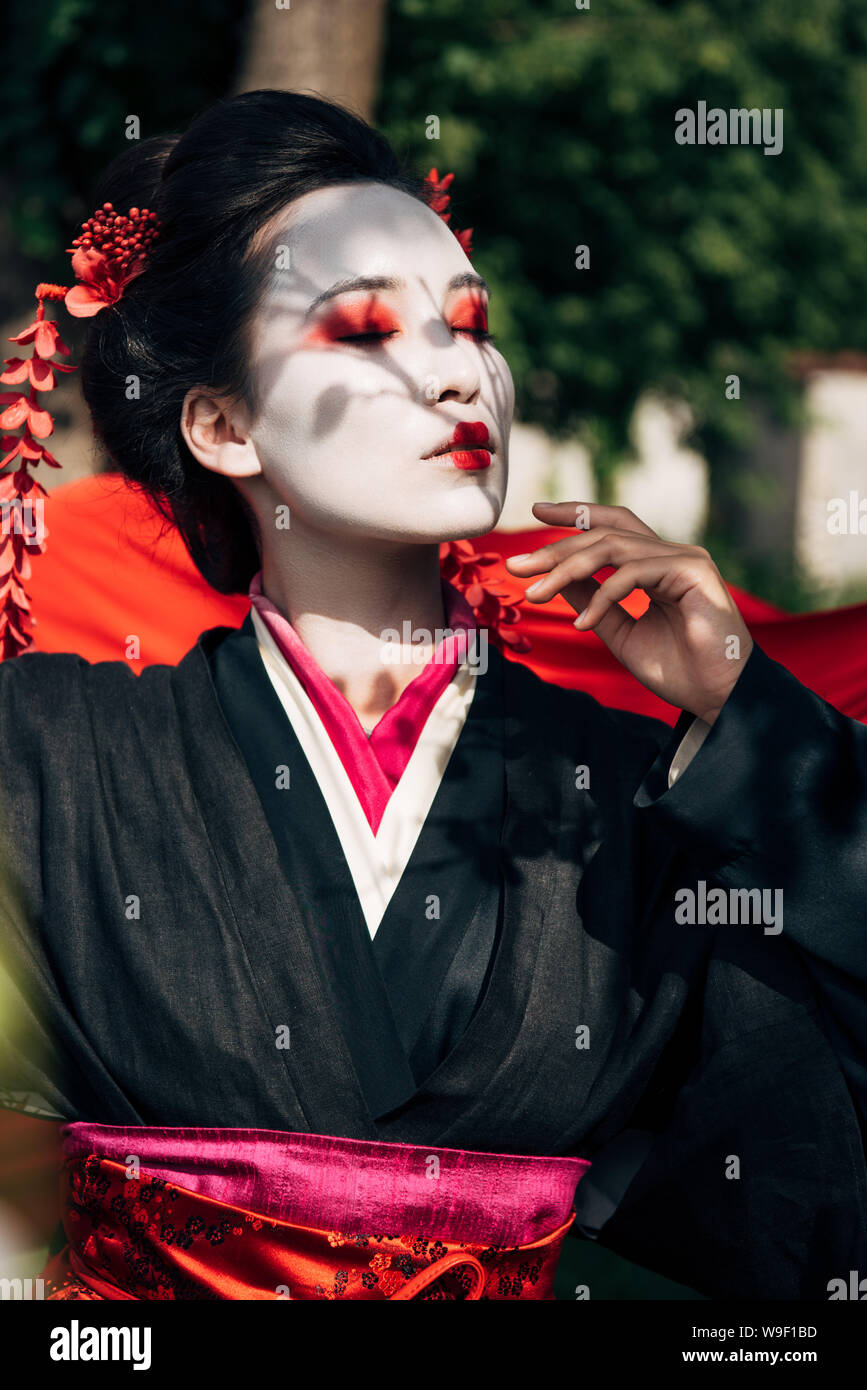 selective focus of tree branches and beautiful geisha with closed eyes ...