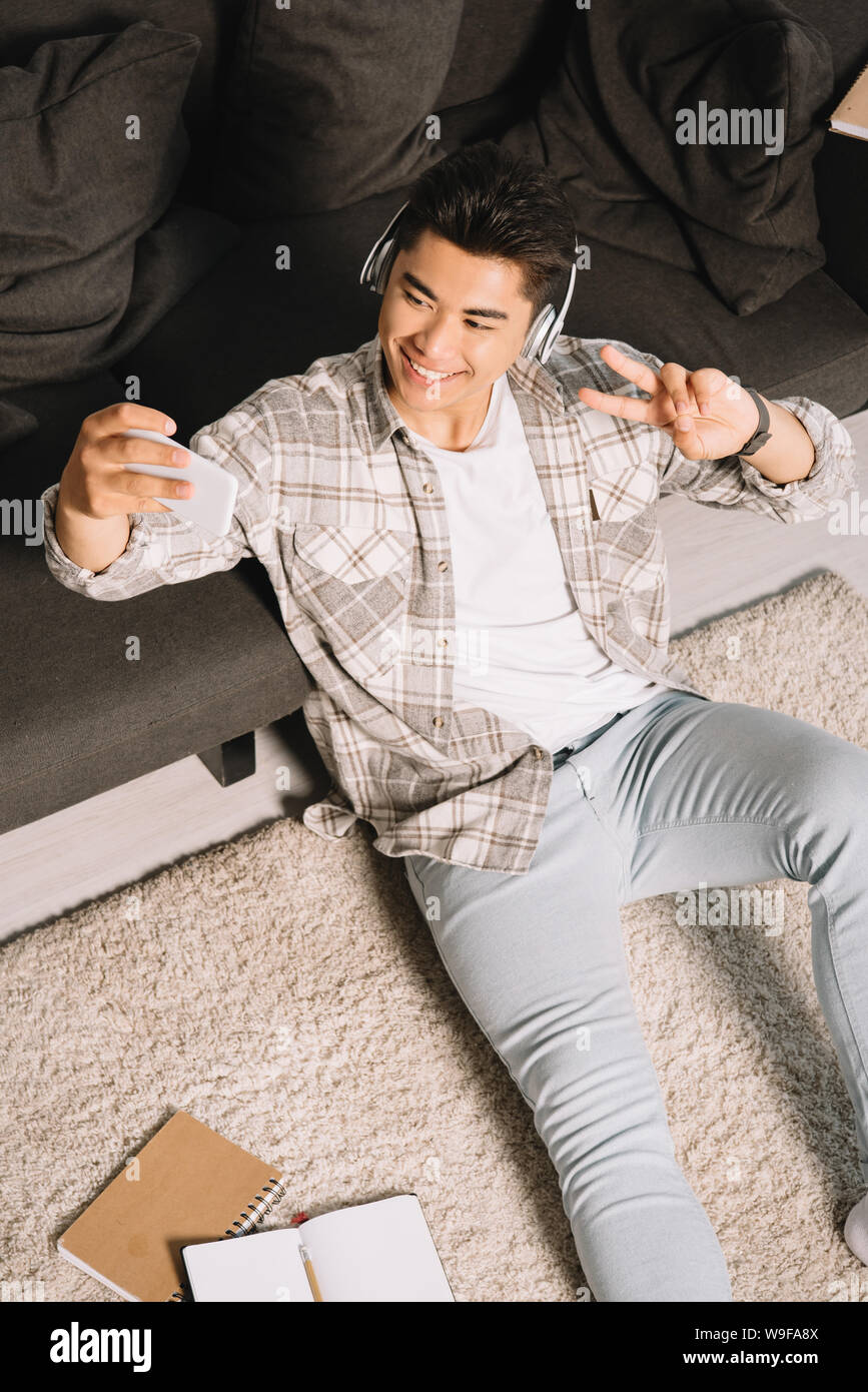 overhead view of cheerful asian man in headphones taking selfie while ...