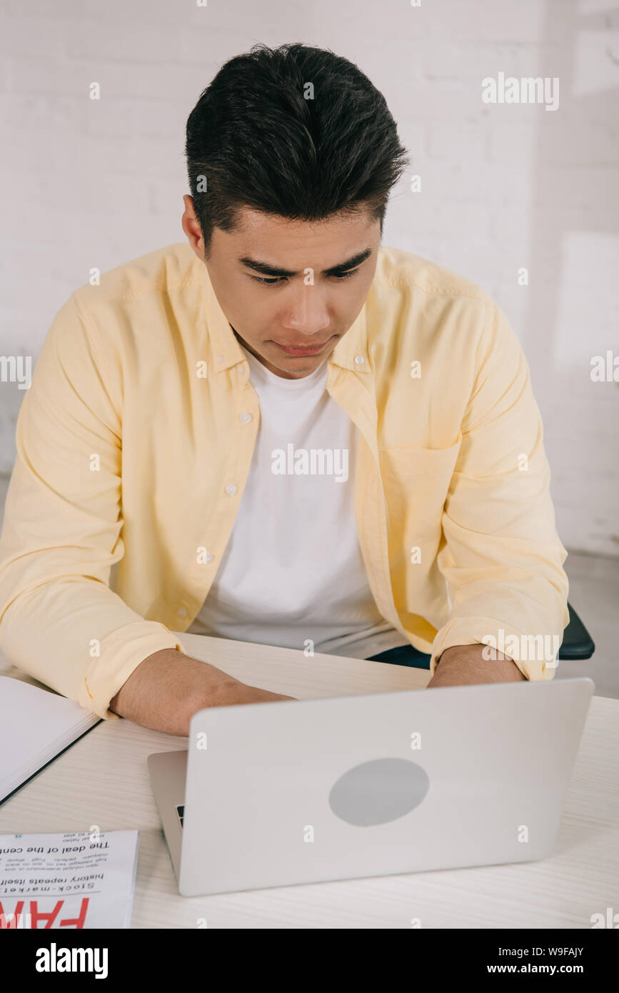 attentive asian man sitting at desk and using laptop at home Stock ...