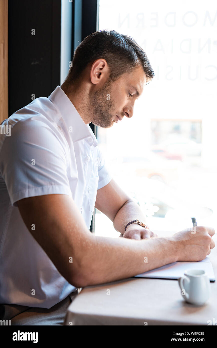 side view of focused handsome man writing in textbook in cafe Stock ...