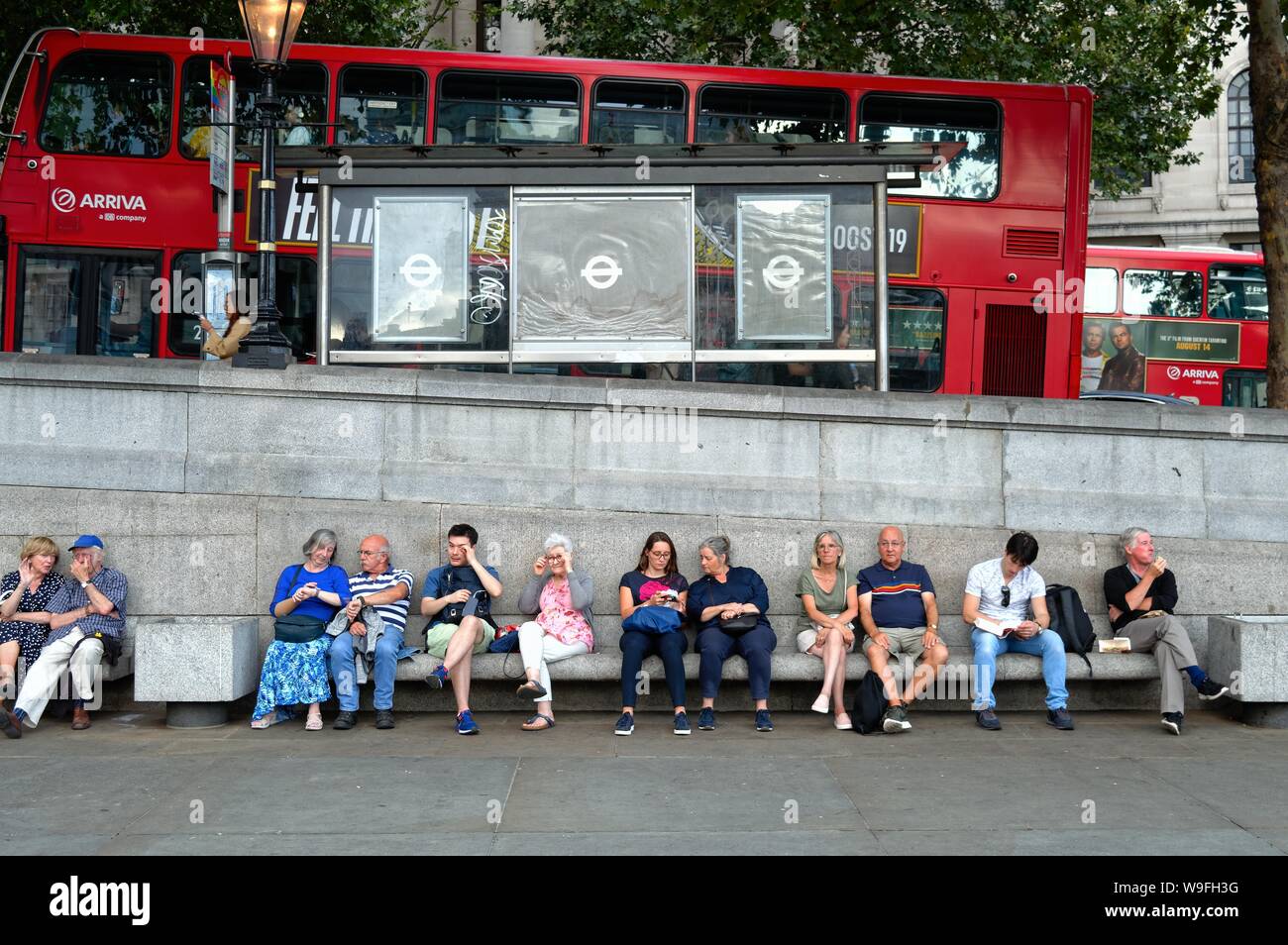 Tired tourists sitting and resting on a bench in Trafalgar Square ...