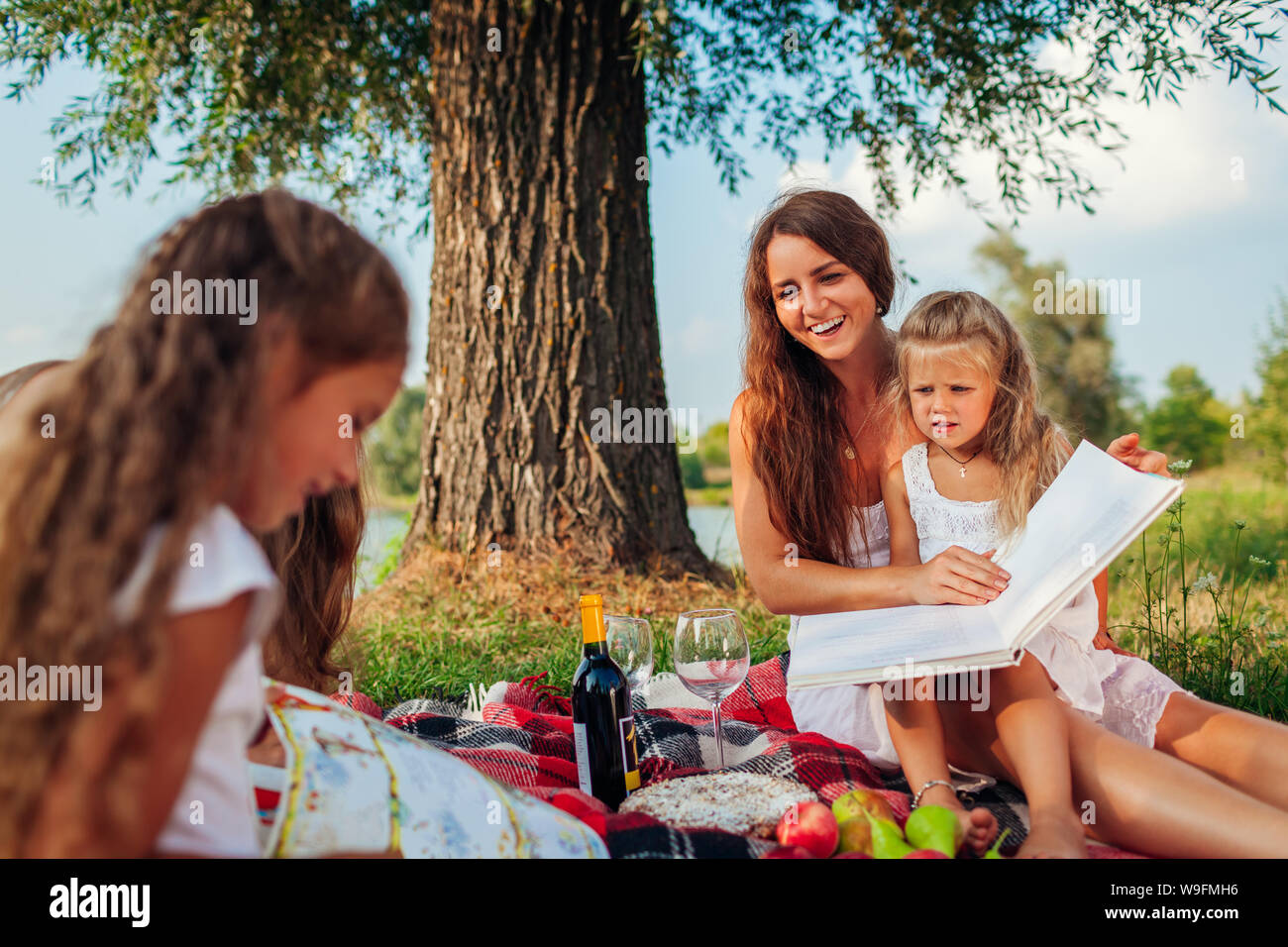 Mother and kids reading books outdoors. Family having picnic in park at ...