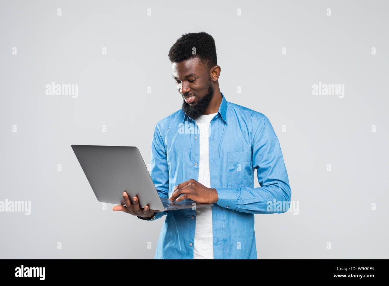 Young smiling african man standing and using laptop computer isolated ...