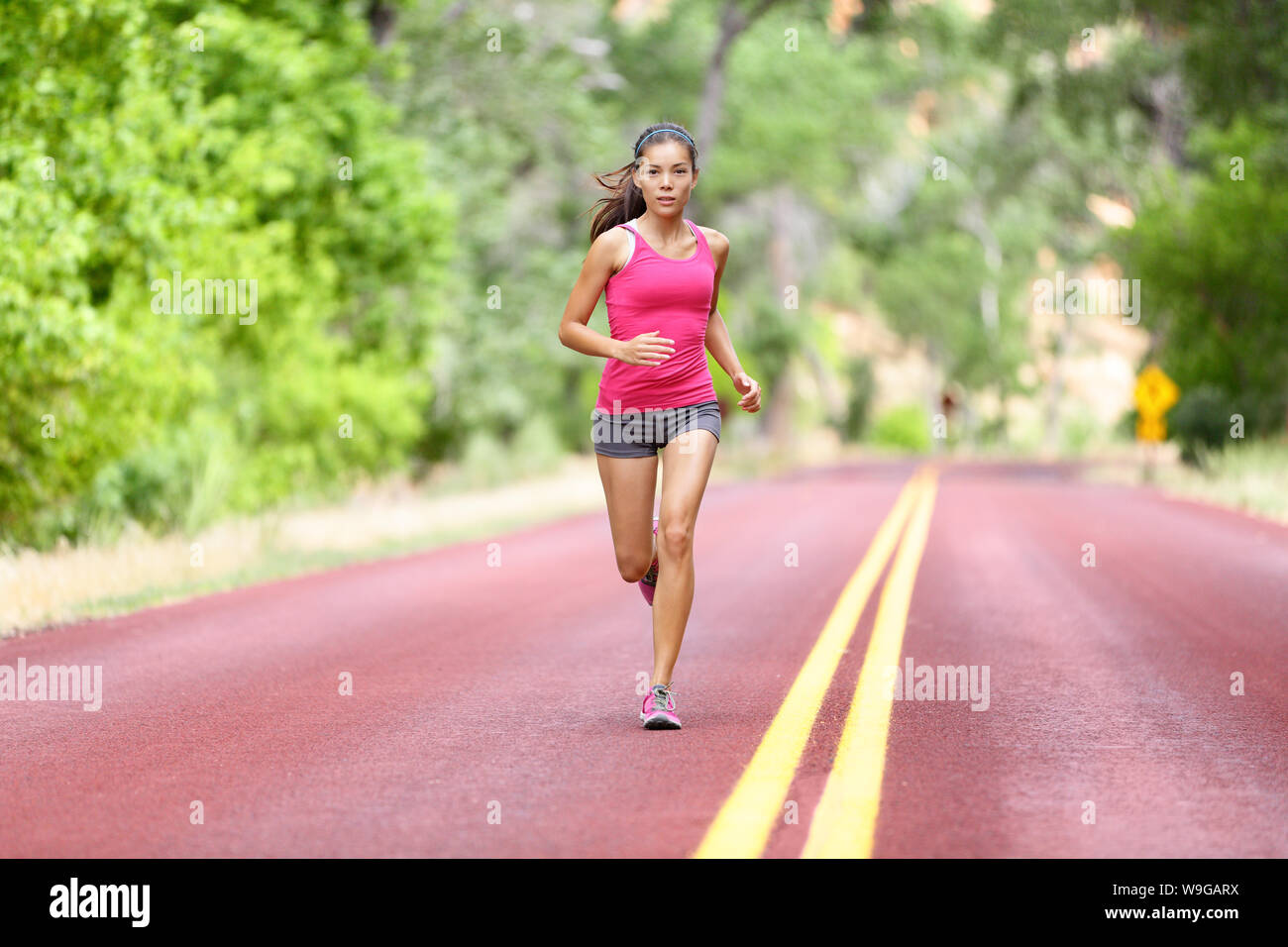 Running fit woman - female runner training outdoors jogging on red road ...